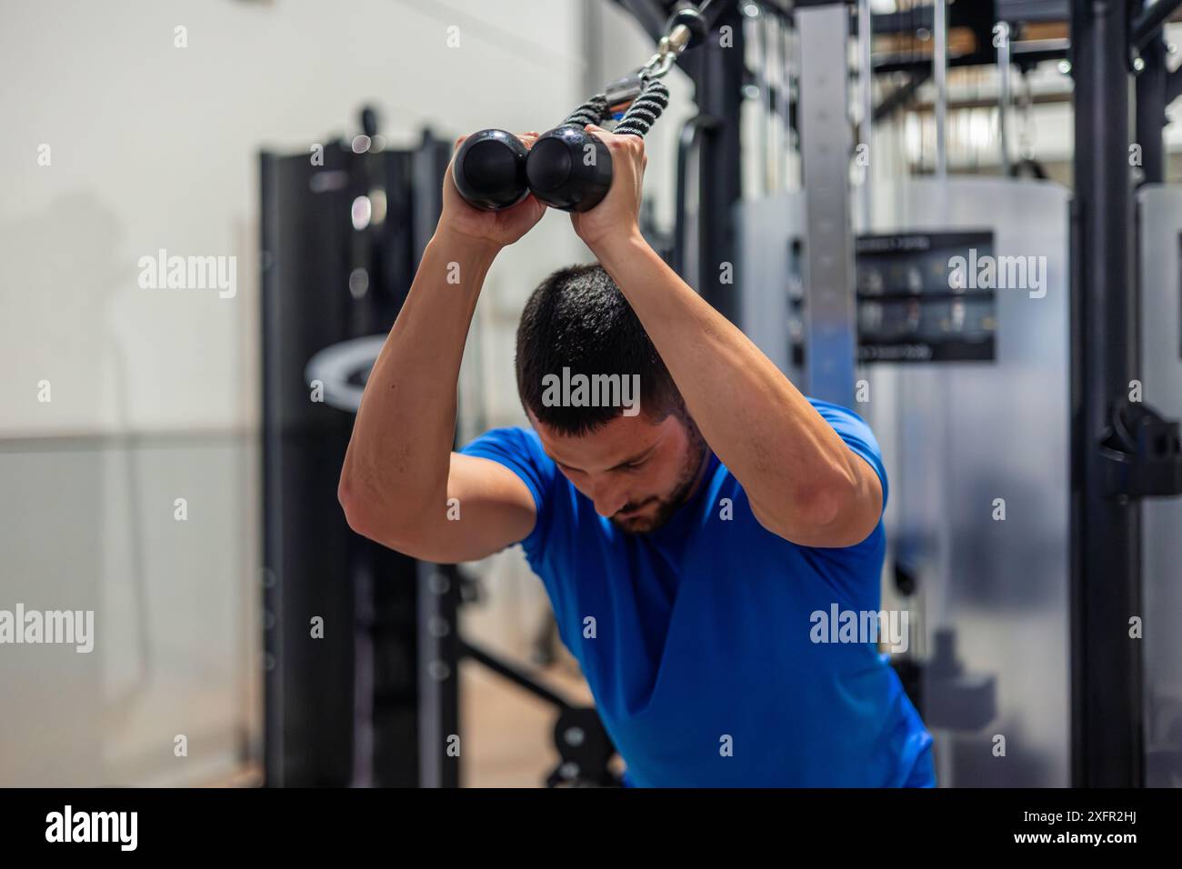 young fitness athlete is using a high pulley machine in the gym to ...