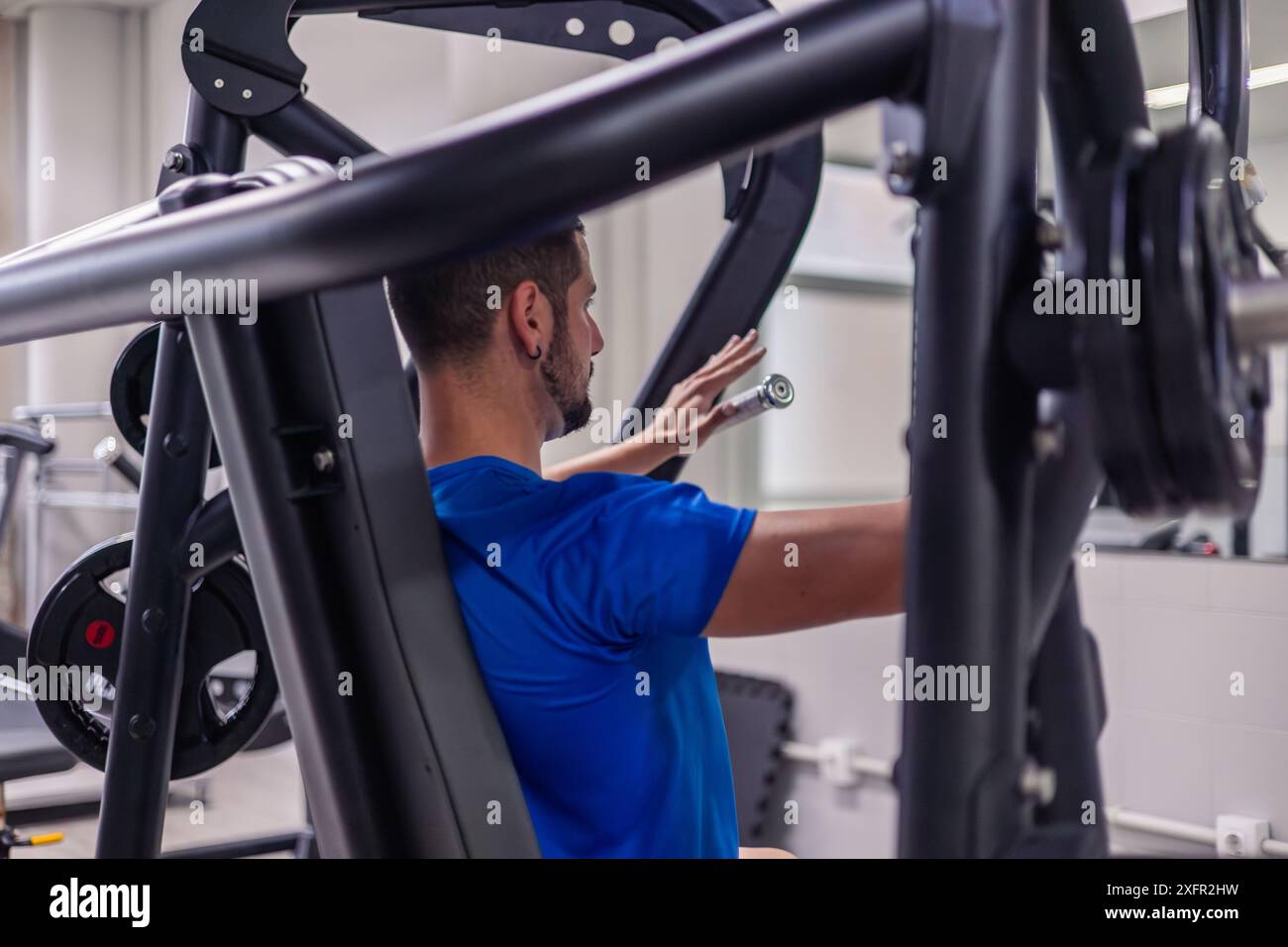 young fitness athlete, seen from behind, is training his chest muscles ...
