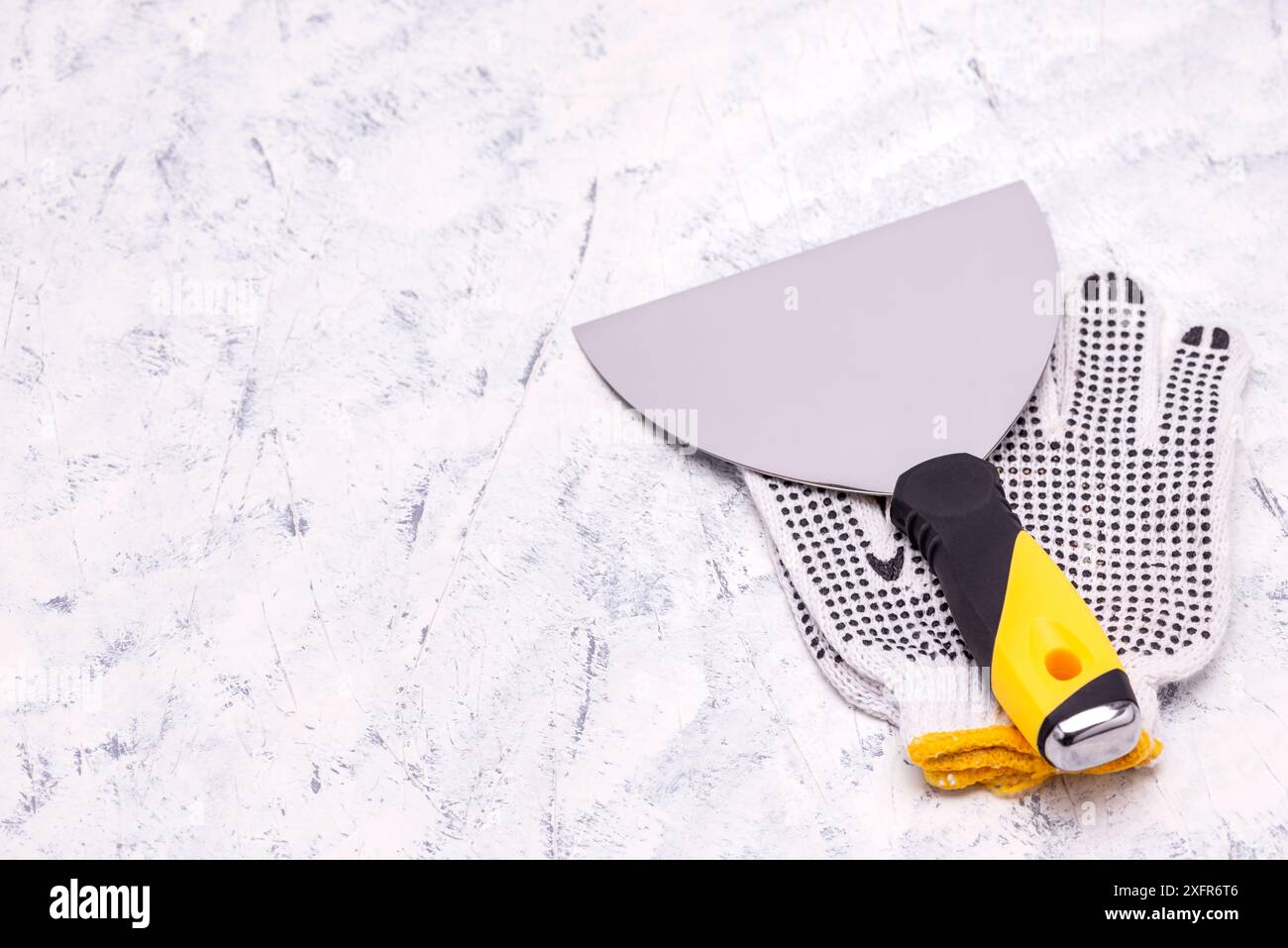 Steel trowel scraper or spatula and protective gloves on white-grey background with copy space ...