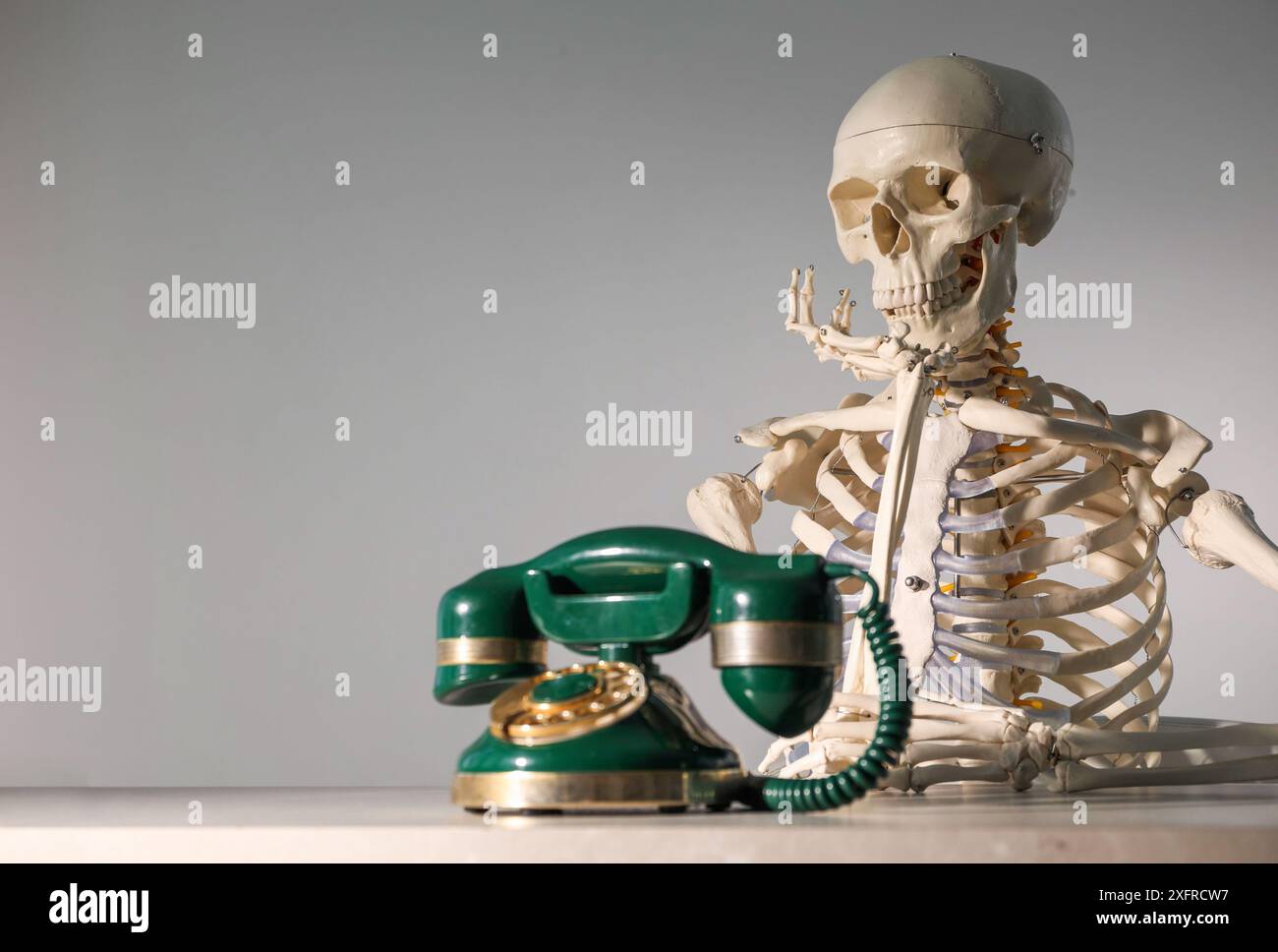 Waiting concept. Human skeleton at table with corded telephone against ...