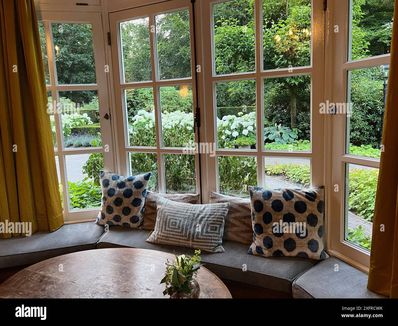 Wooden table near bay window seat with cushions in cozy room. Interior ...