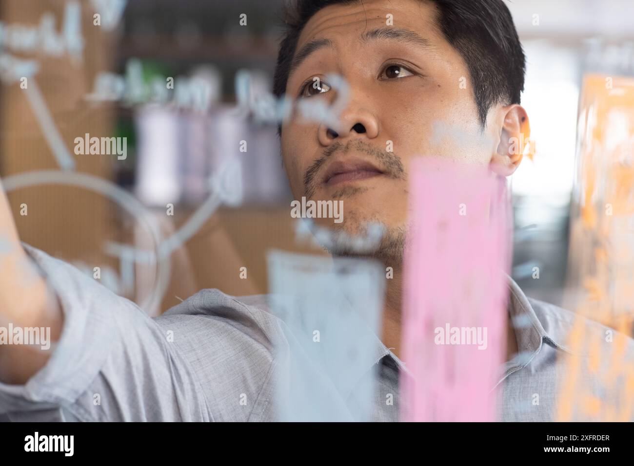 Writing on transparent board, man focusing on project planning and ...