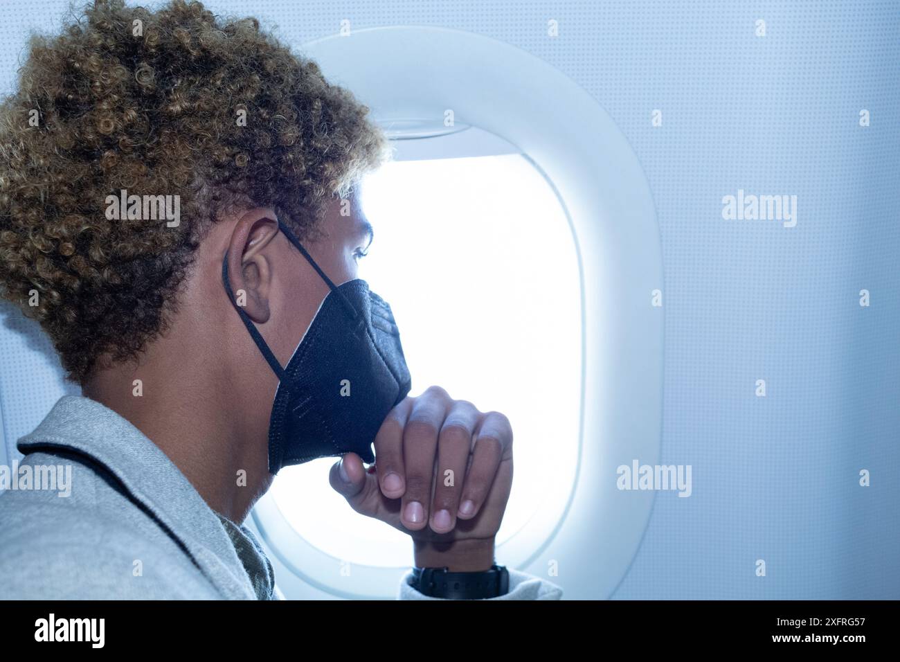 A traveler afro teen is staring out of an airplane window while wearing ...