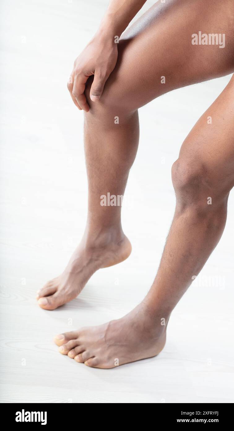 man is pressing his thigh with one hand, suggesting leg pain. His feet ...
