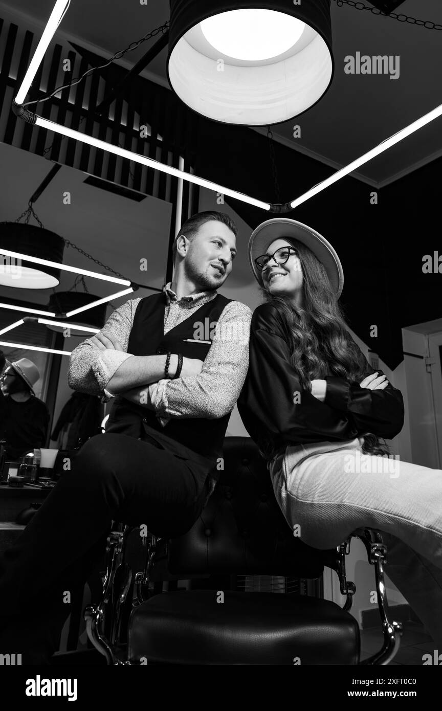 A couple of barbers look at each other sit on a chair in a modern ...