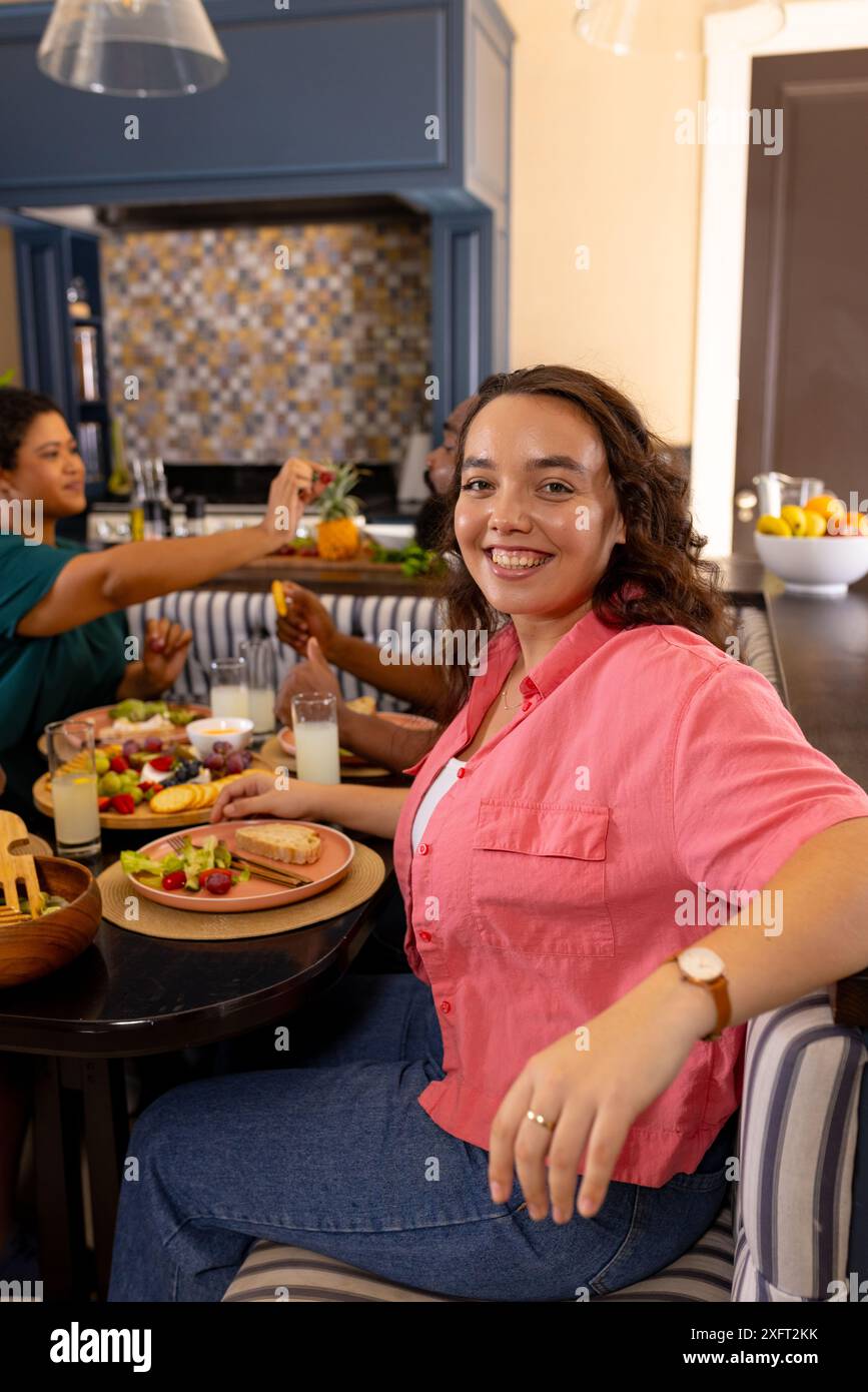 Smiling woman sitting at dining table with diverse friends enjoying ...