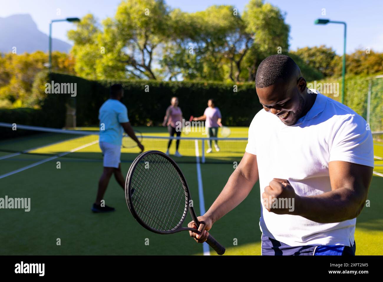 Celebrating victory, man holding tennis racket with diverse friends ...