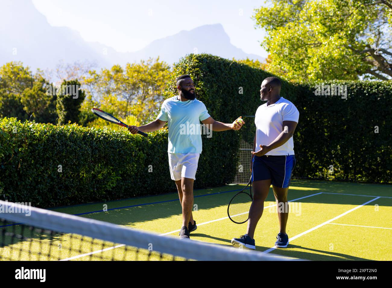 Playing tennis, two diverse friends holding rackets and talking on ...