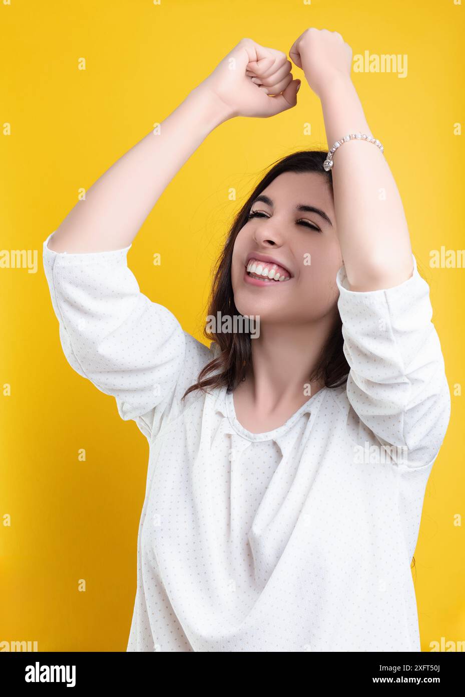Young woman is raising her arms in the air and smiling with her eyes ...