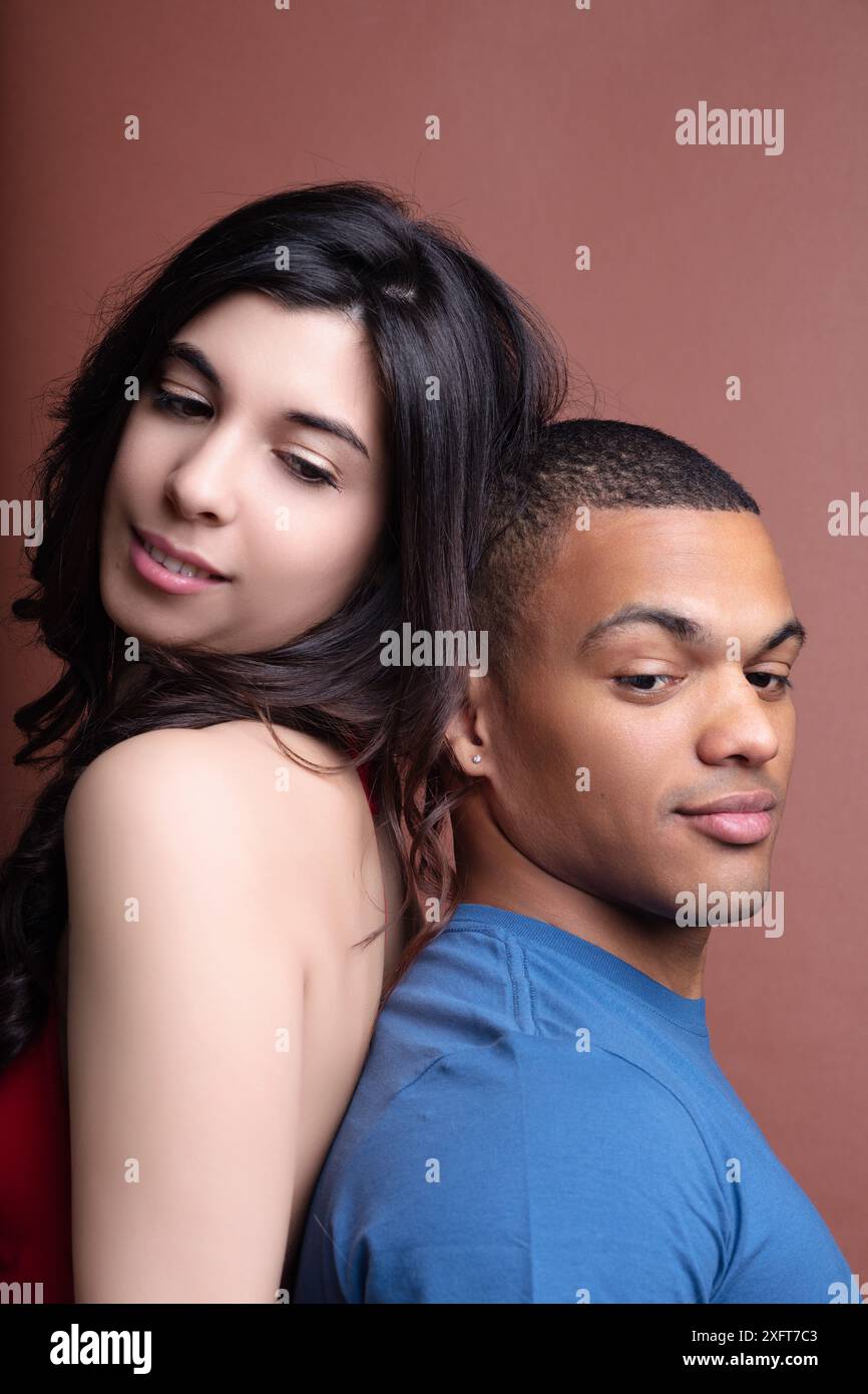 Young couple is posing back to back, with the woman slightly leaning on ...