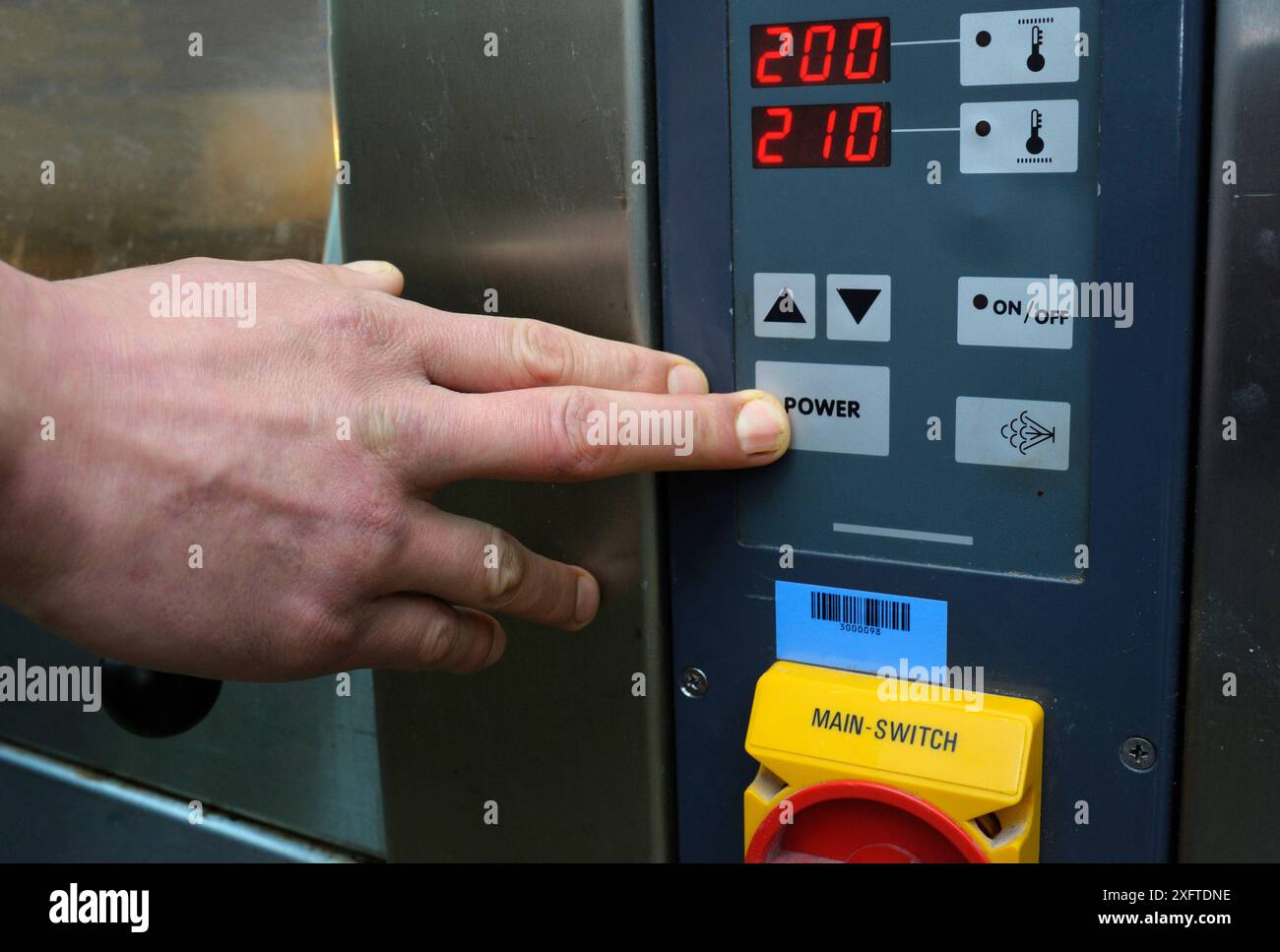 worker baker hand pressing power button on a control panel of an ...