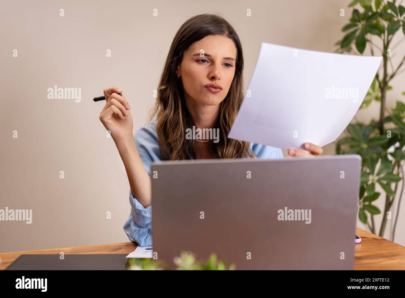 A focused woman reviewing documents at her desk in a home office ...