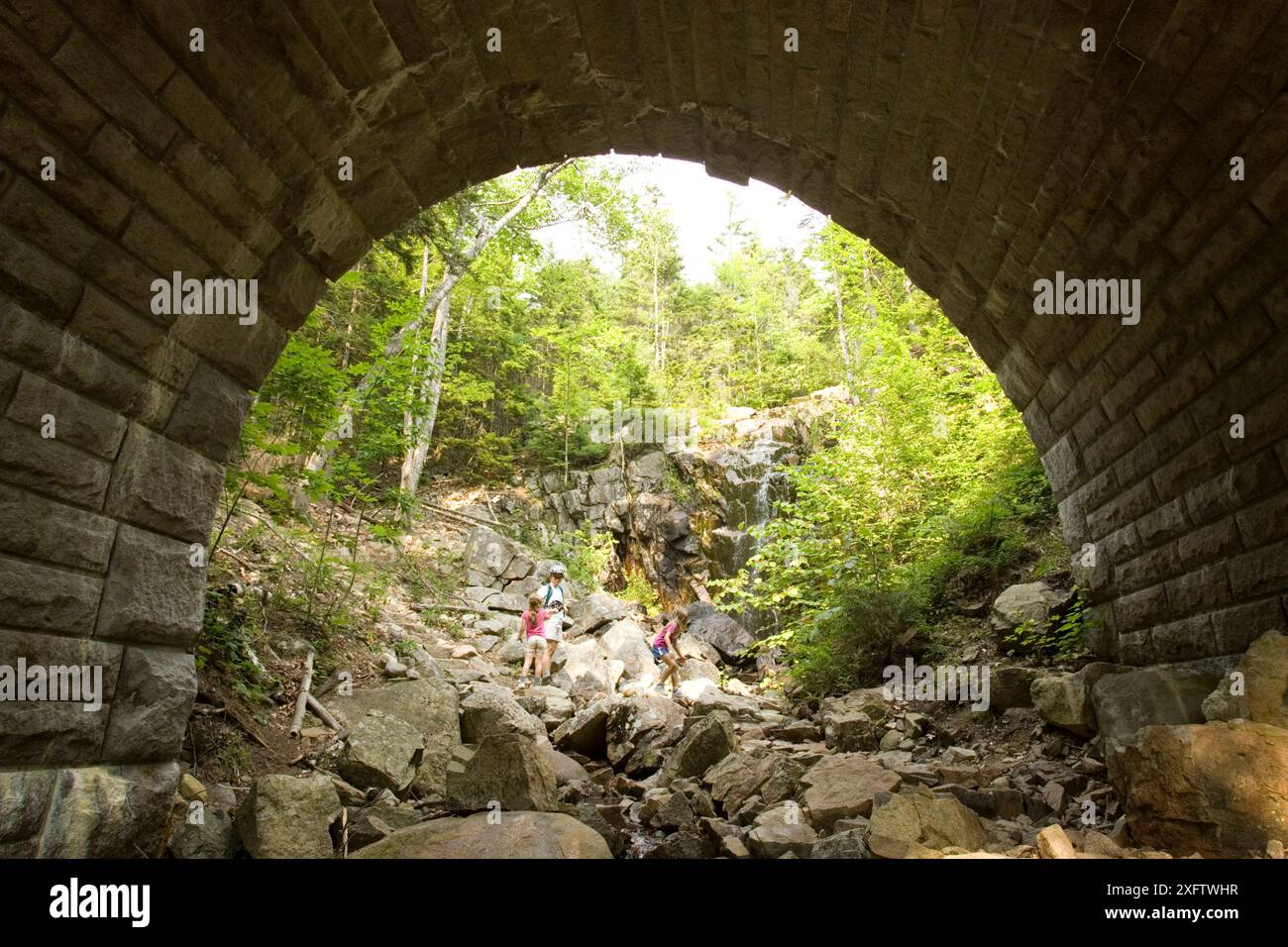 A family hikes underneath a stone bridge along the carriage roads at ...