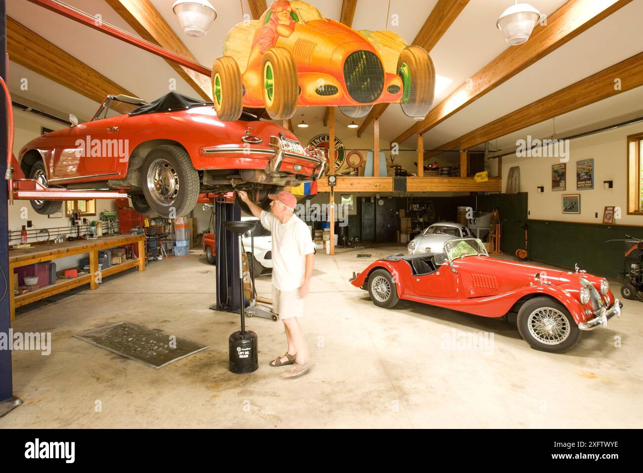 A man repairs one of his antique sports cars on a lift inside a garage ...