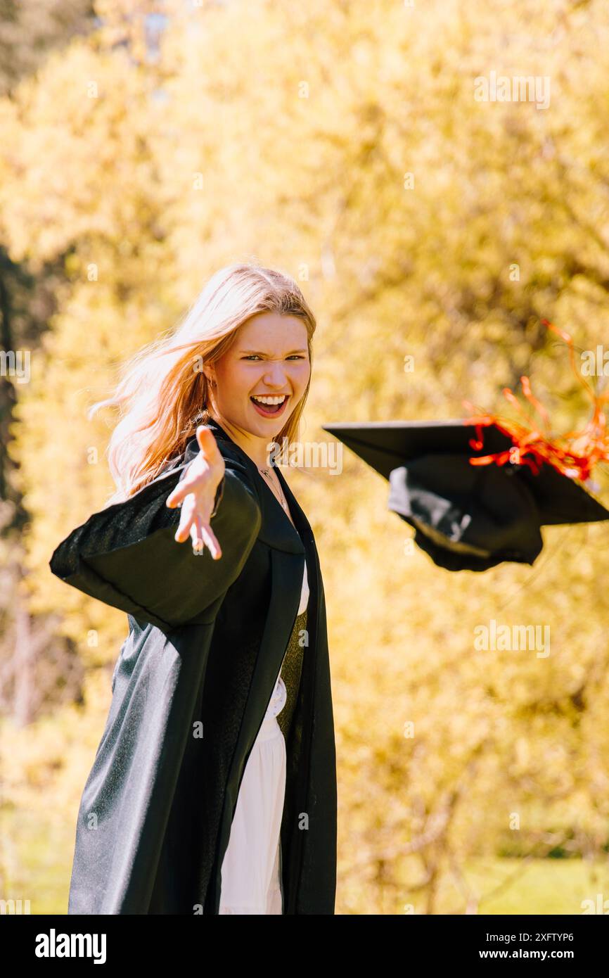 Happy graduate throwing her cap outdoors with bright yellow foli Stock ...