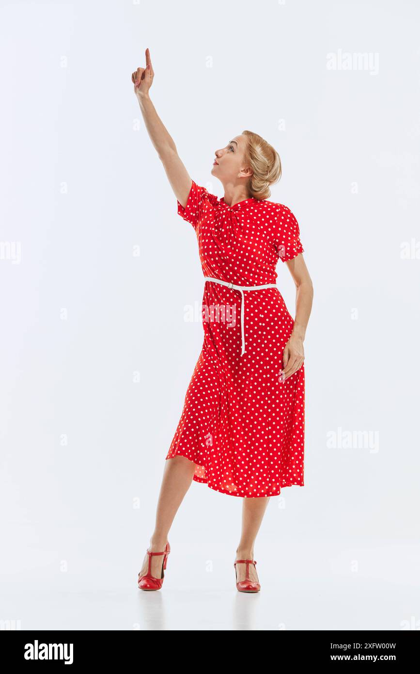 Elegant woman in red polka dot dress and matching heels points upwards ...