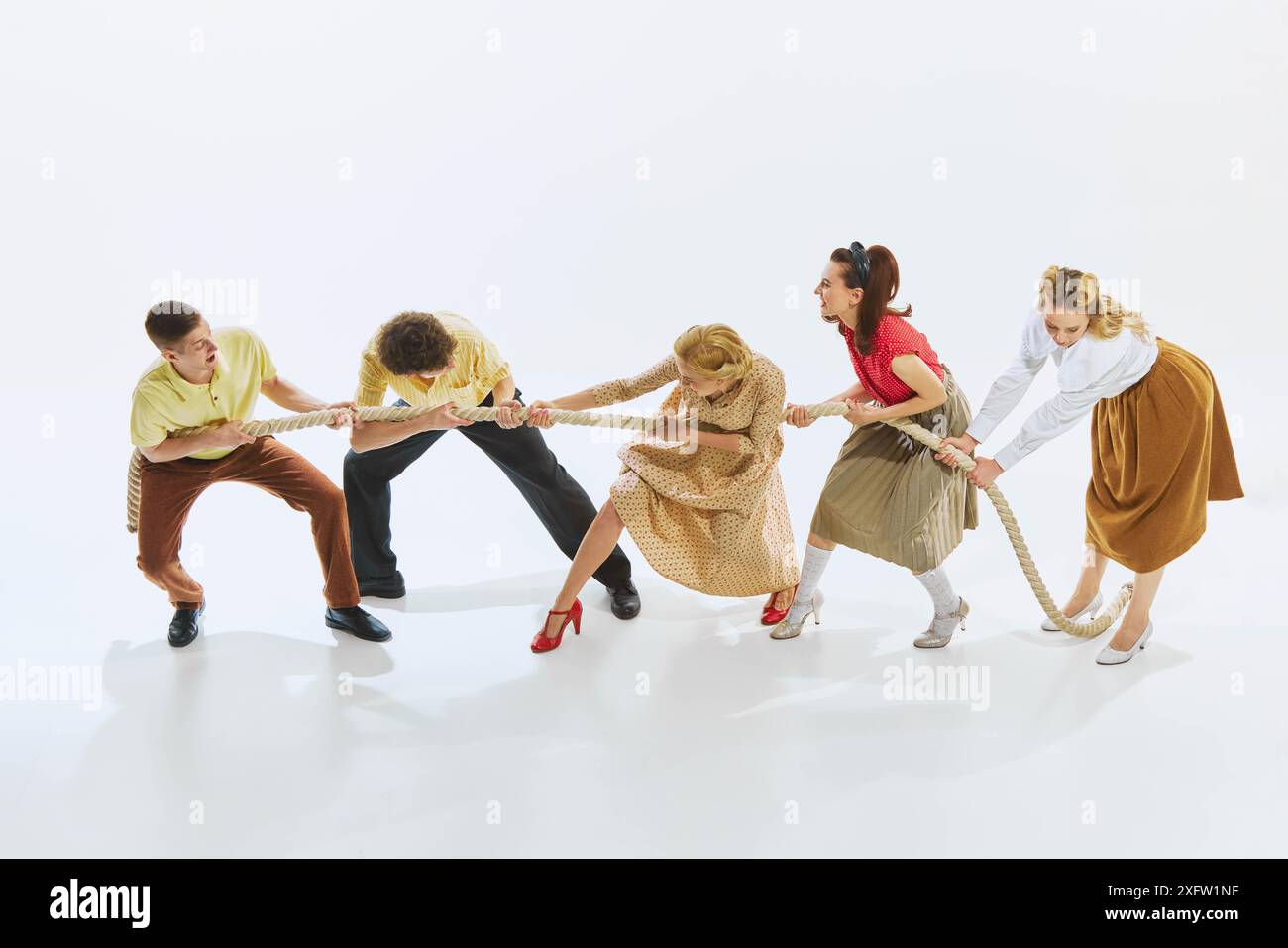 Group of men and women in vintage clothing engage in lively game of tug-of-war. People pulling ...