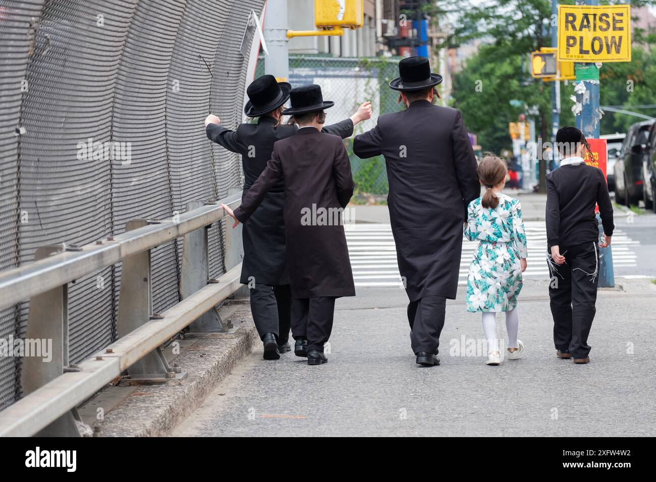 A view from behind of a Hasidic father & 4 children walking south on ...