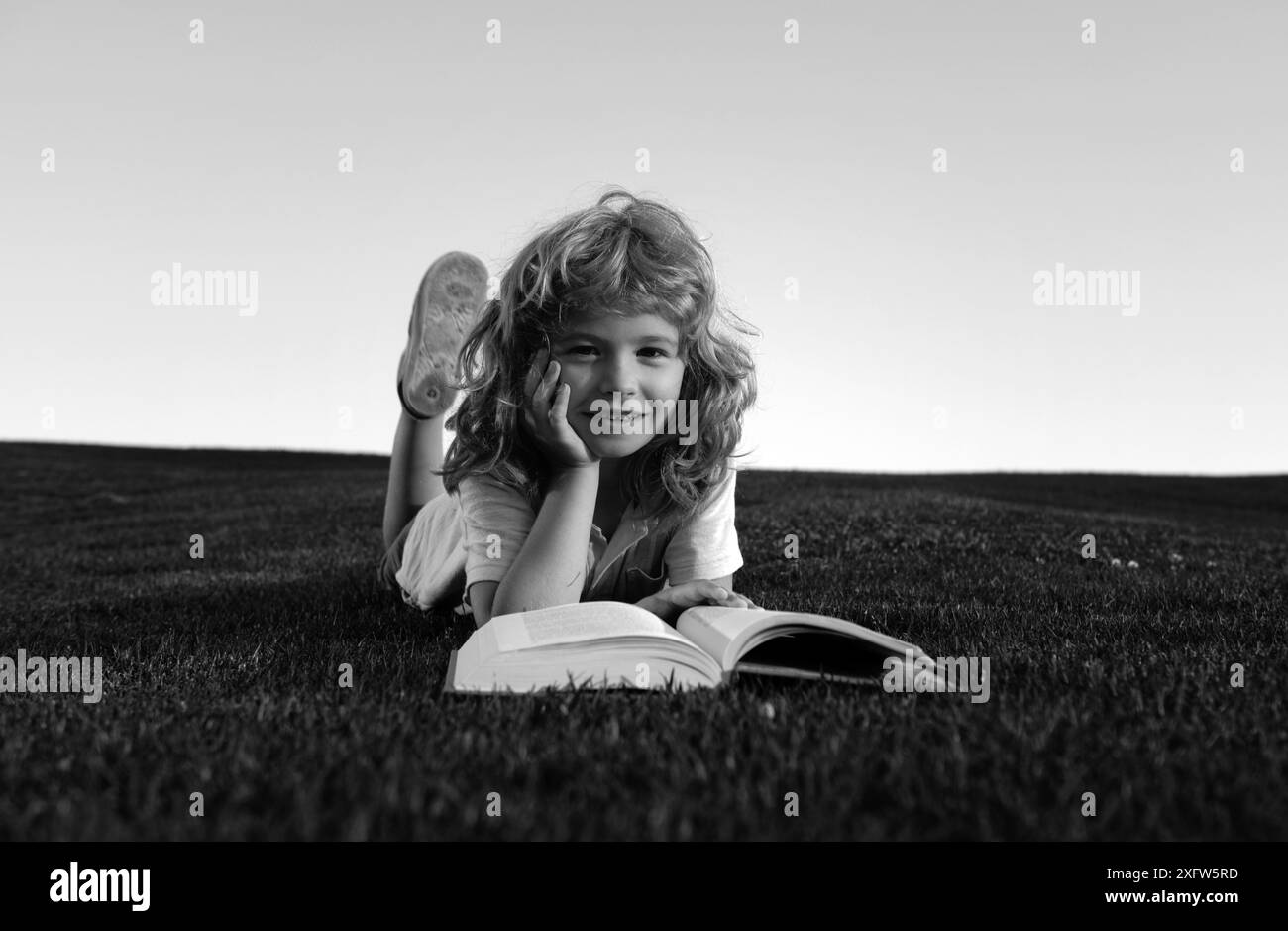 Clever child boy reading book laying on grass on grass and sky ...