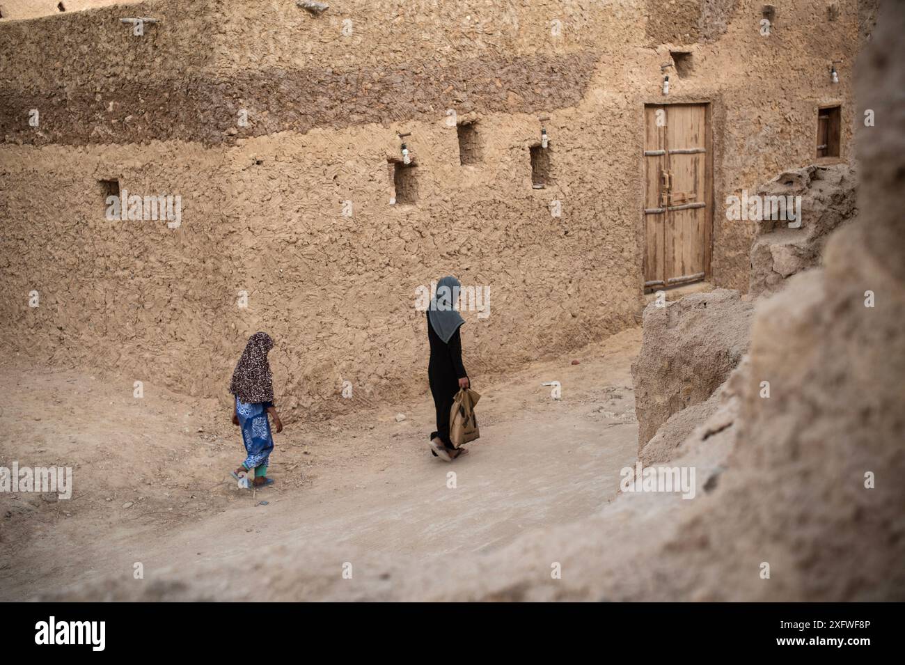 A woman and child walk through the traditional mud brick buildings of ...