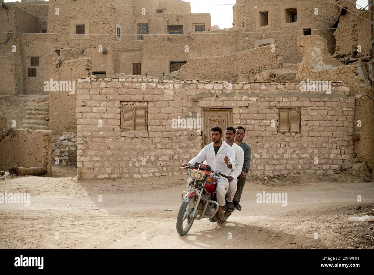 Three Egyptian men riding a motorcycle in the ruins of Shali fortress ...