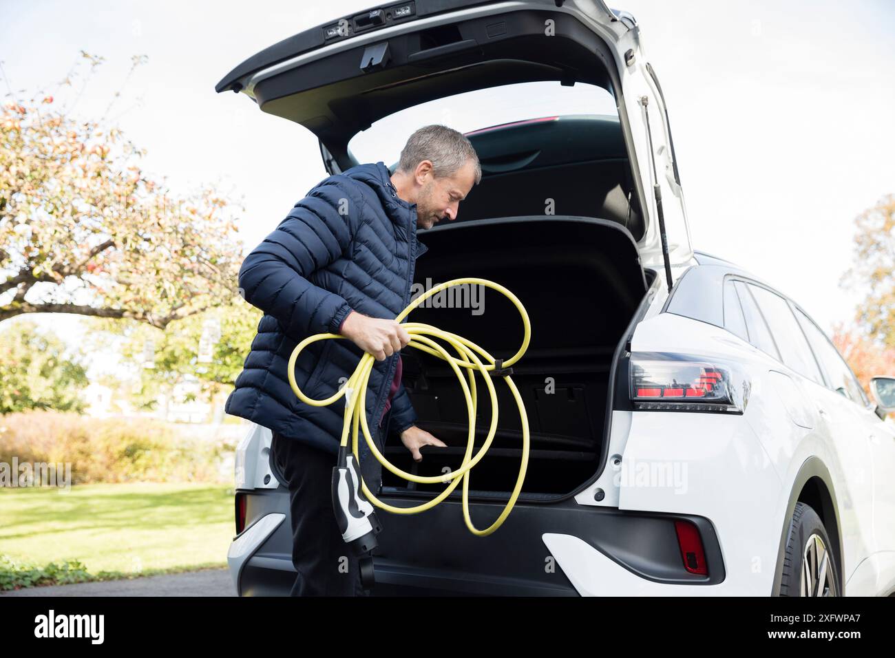 Man removing charging cable from trunk of electric car Stock Photo - Alamy