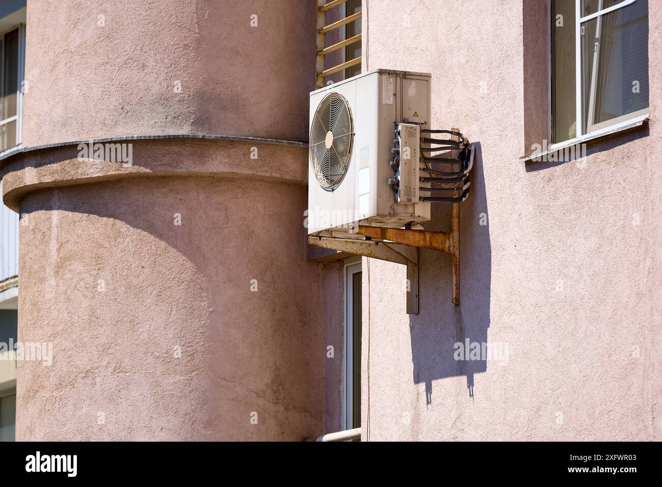 Old air conditioning heat pump outdoor unit against rose wall ...