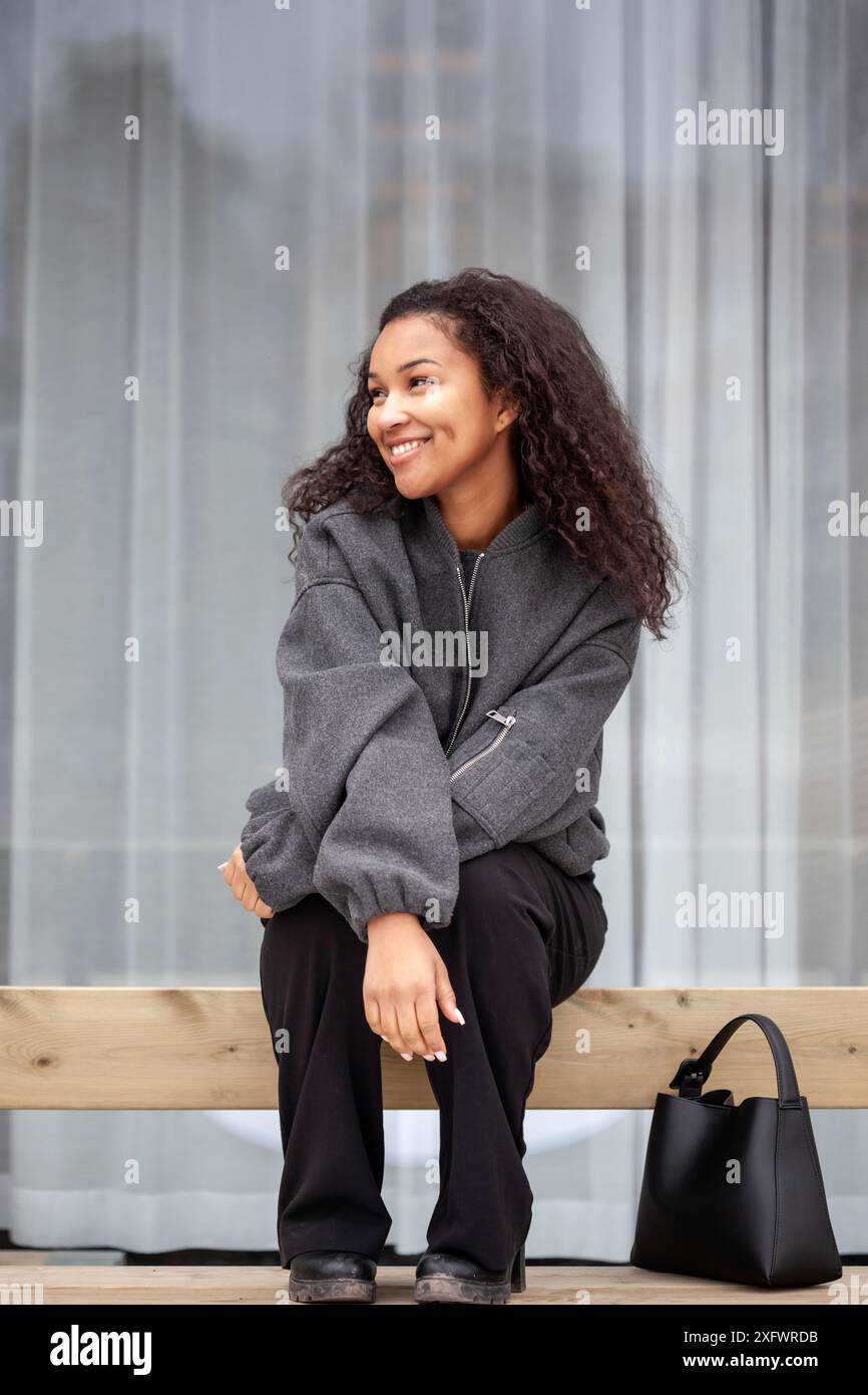 Smiling young woman carrying sitting on bench Stock Photo - Alamy