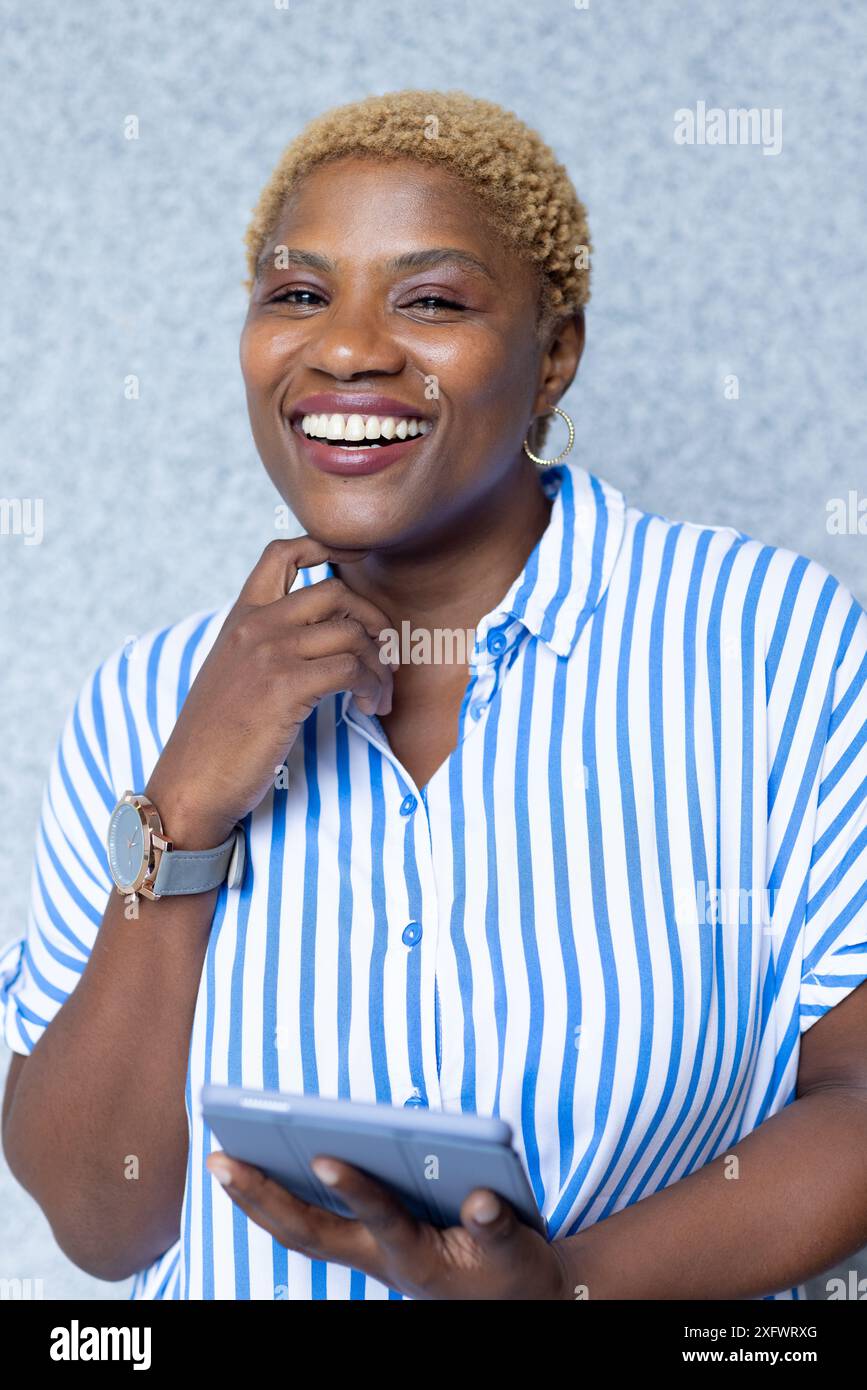 Smiling african american woman holding tablet and wearing striped shirt ...