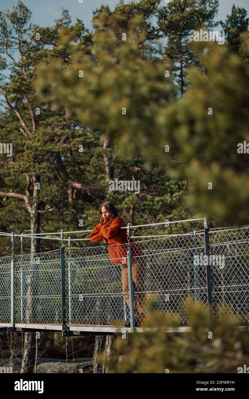 Thoughtful young woman leaning on railing while standing on bridge ...