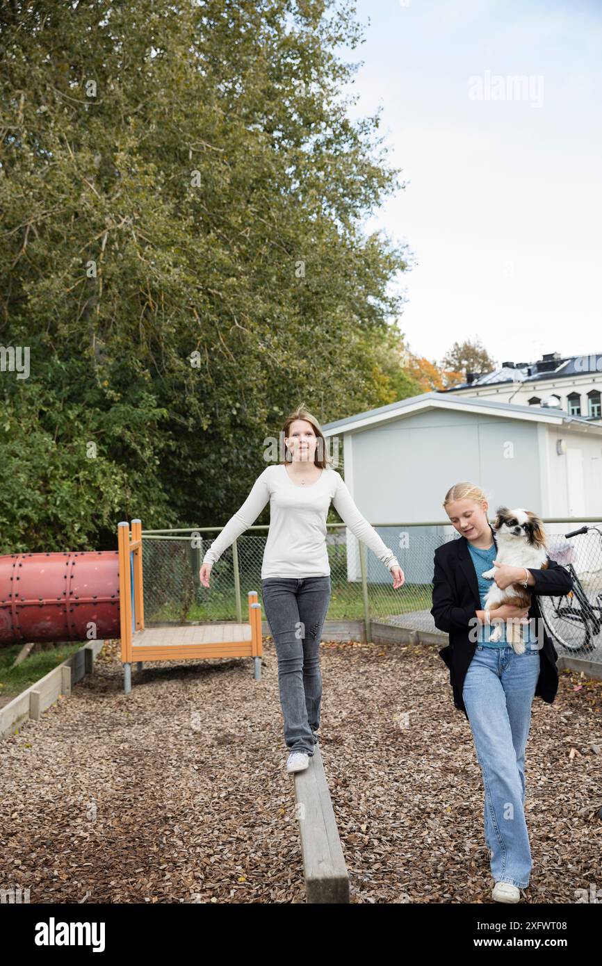 Teenage girls playing on log of wood at schoolyard Stock Photo - Alamy