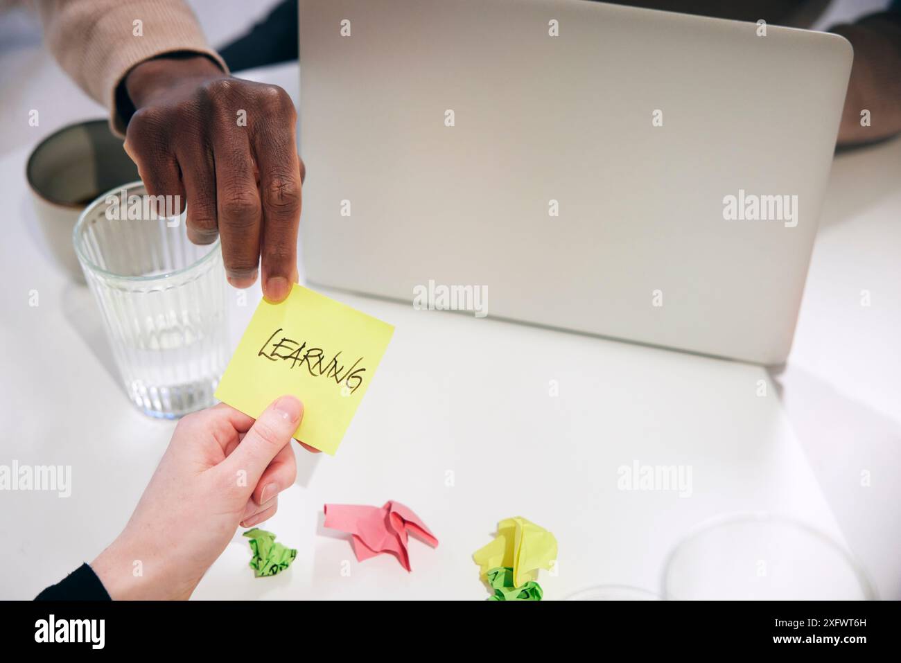 Cropped hands of colleagues sharing adhesive note with text learning by ...