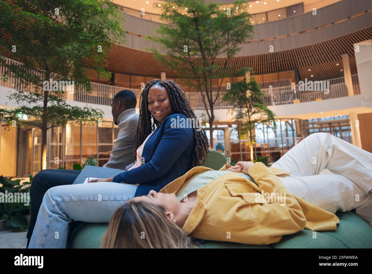 Female employee relaxing on couch with office colleagues sitting in ...