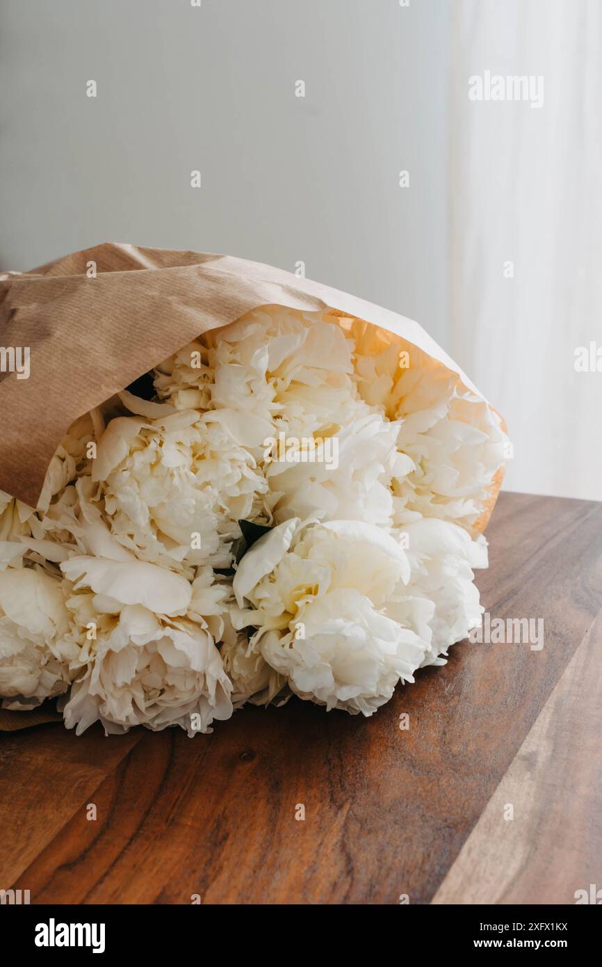 Bouquet of white peony flowers in a craft paper on brown wooden table ...