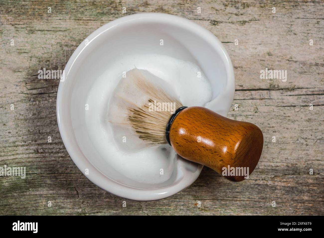 Horizontal photo of macro of lathered boar shaving brush in ceramic bowl, resting in rustic ...