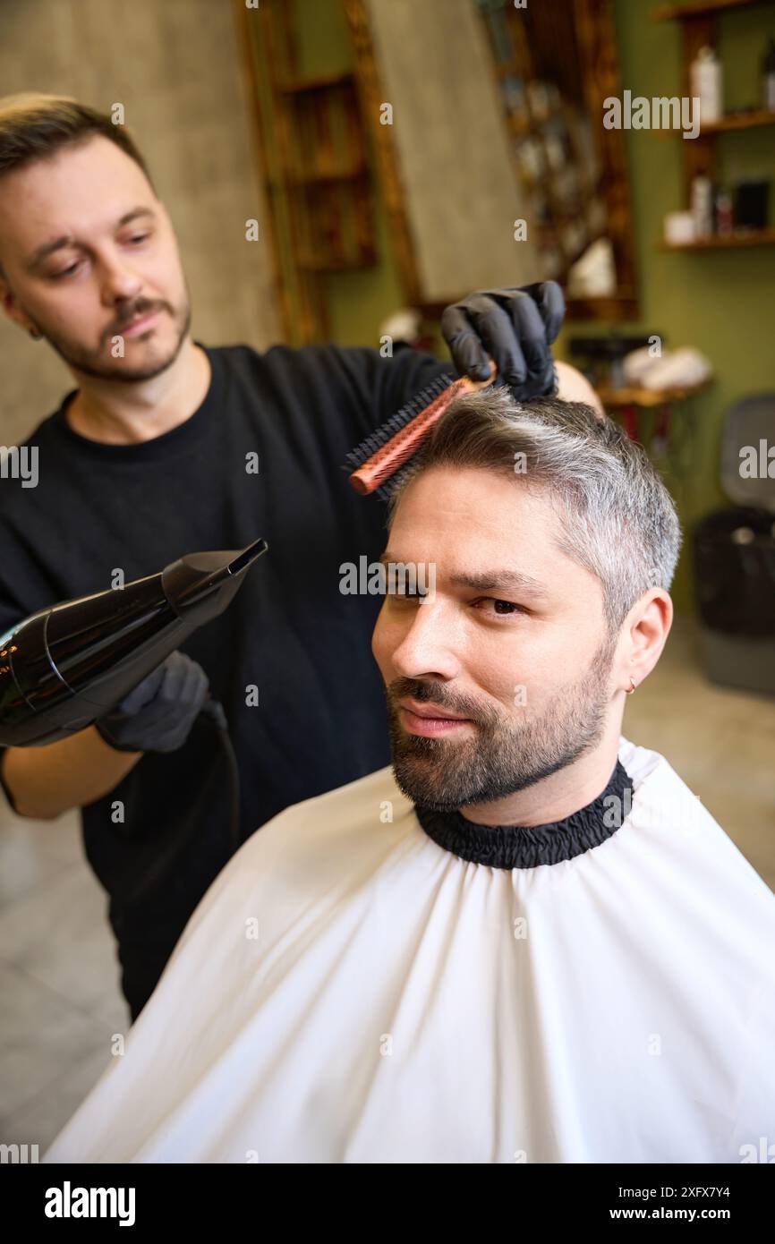 Self-confident man looking camera while hair stylist working on his ...