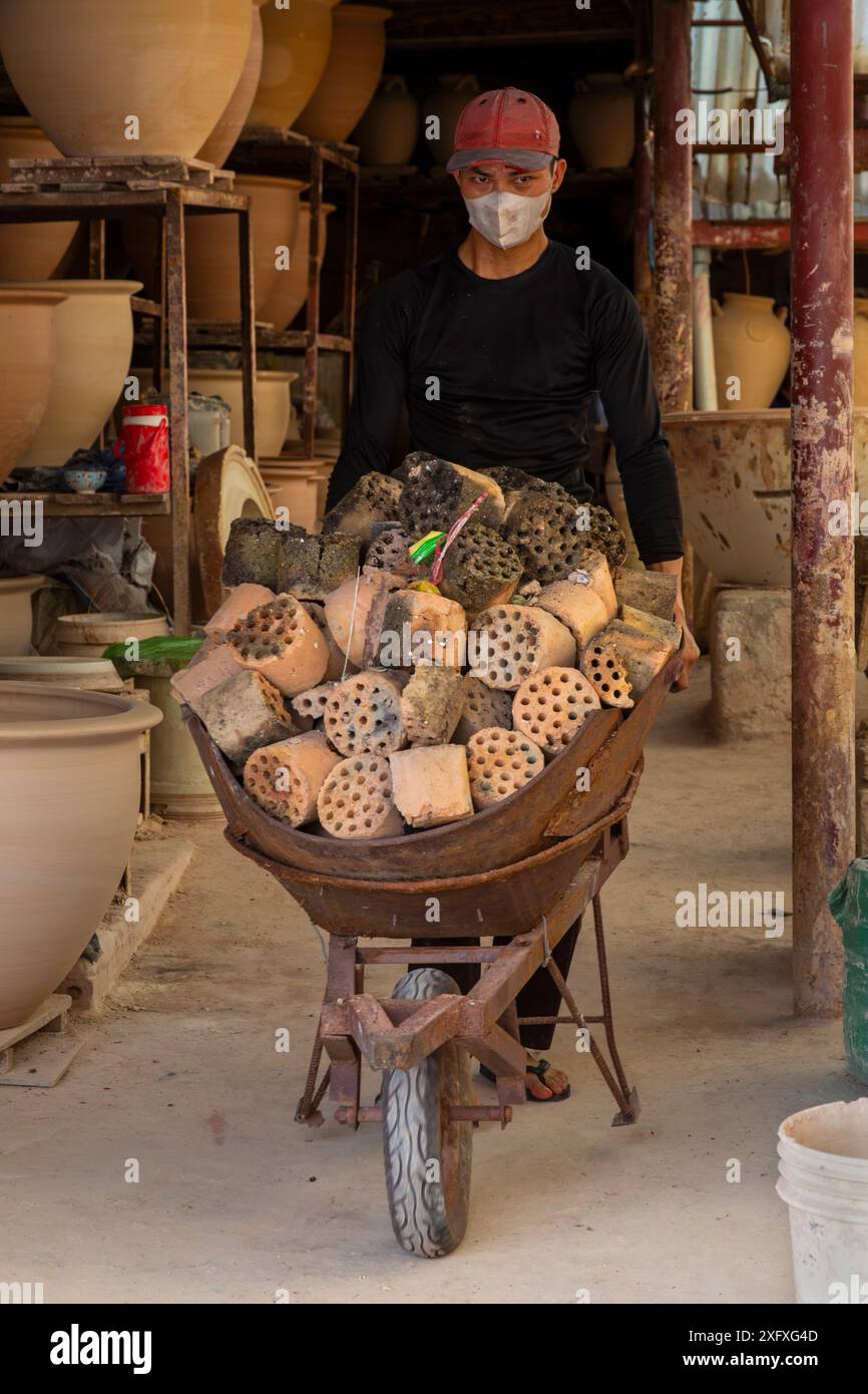 Man moving in fire clay bricks wheelbarrow at clay pot factory at Dong ...