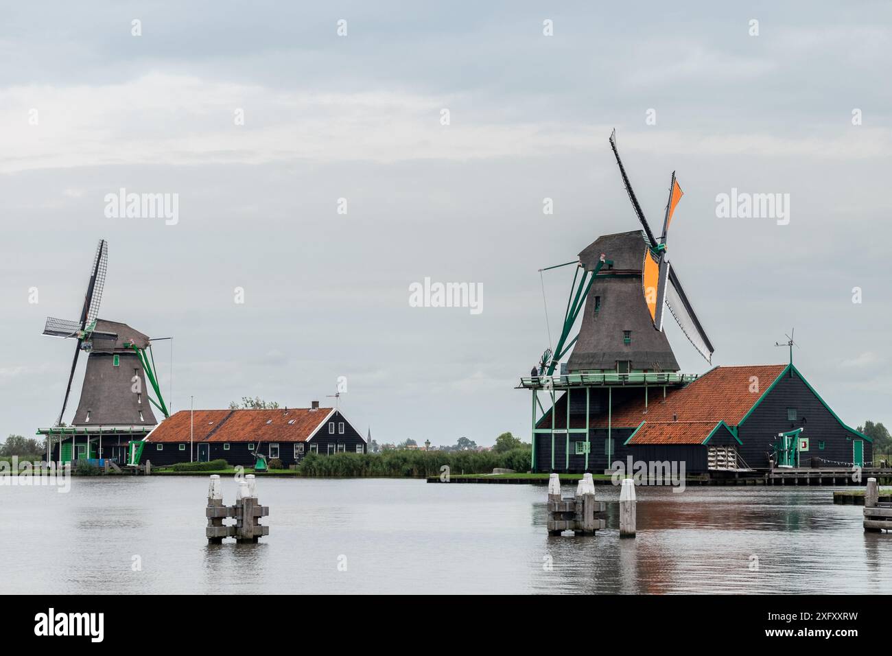 Two windmills are on the water next to a house. The windmills are tall ...