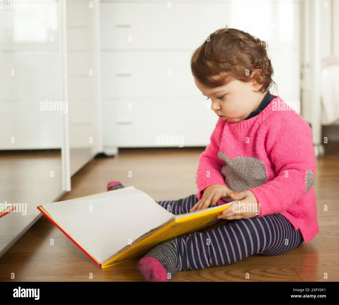 Toddler baby girl playing with fairy tales book on the oak wood floor ...