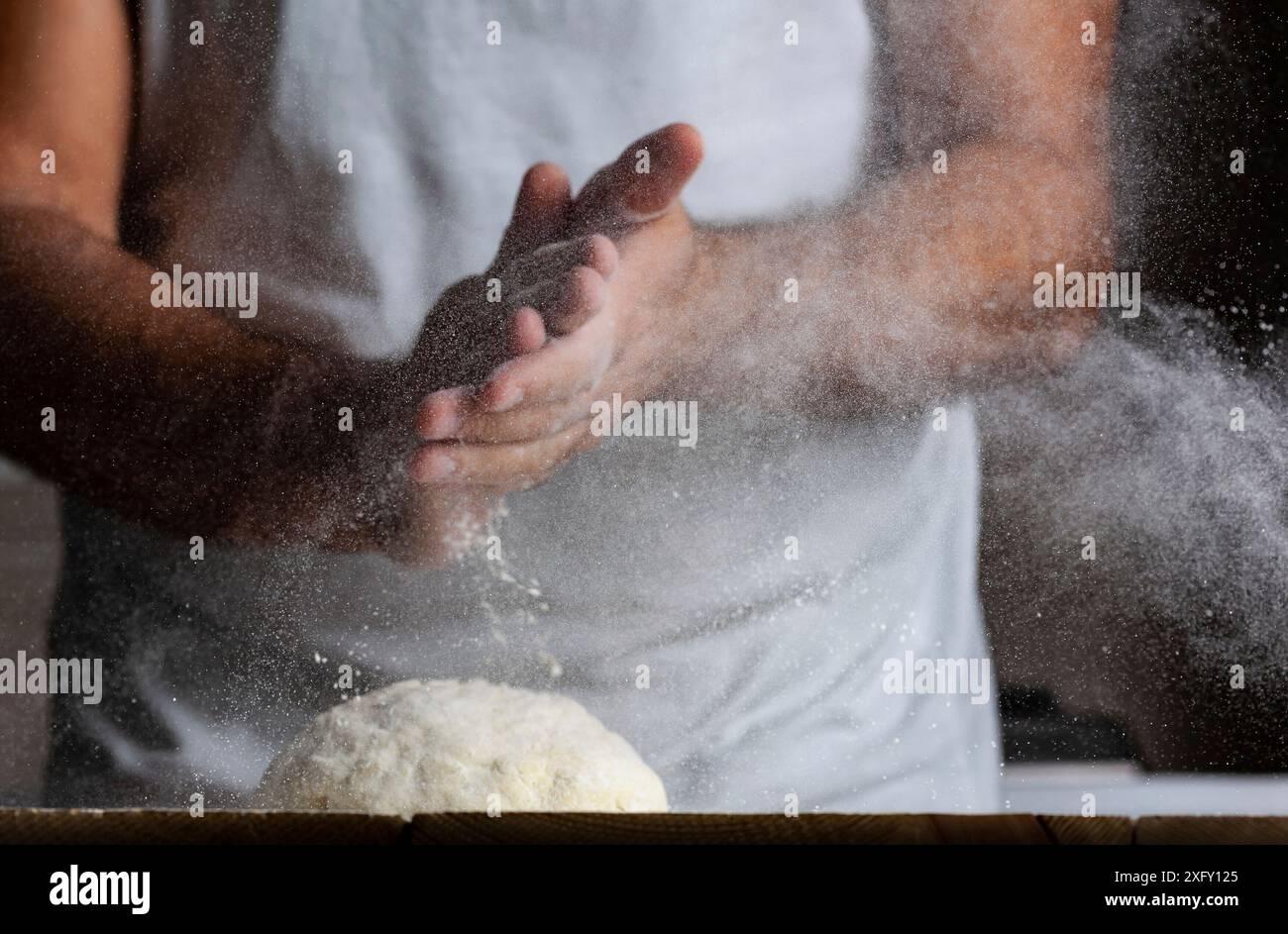 Man kneads raw dough, dust from flour flies in different directions ...