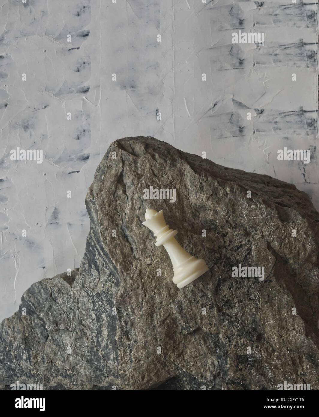 White queen chess piece laying on a rock, with white painted background ...