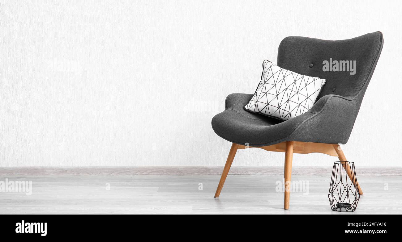 Stylish grey armchair, cushion and lantern near white wall. Banner for ...