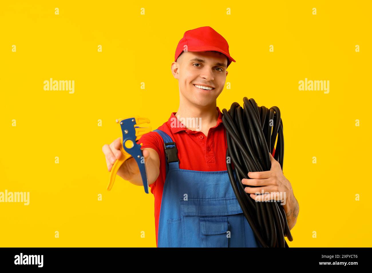 Young male electrician with wire stripper and flexible conduit tube on ...
