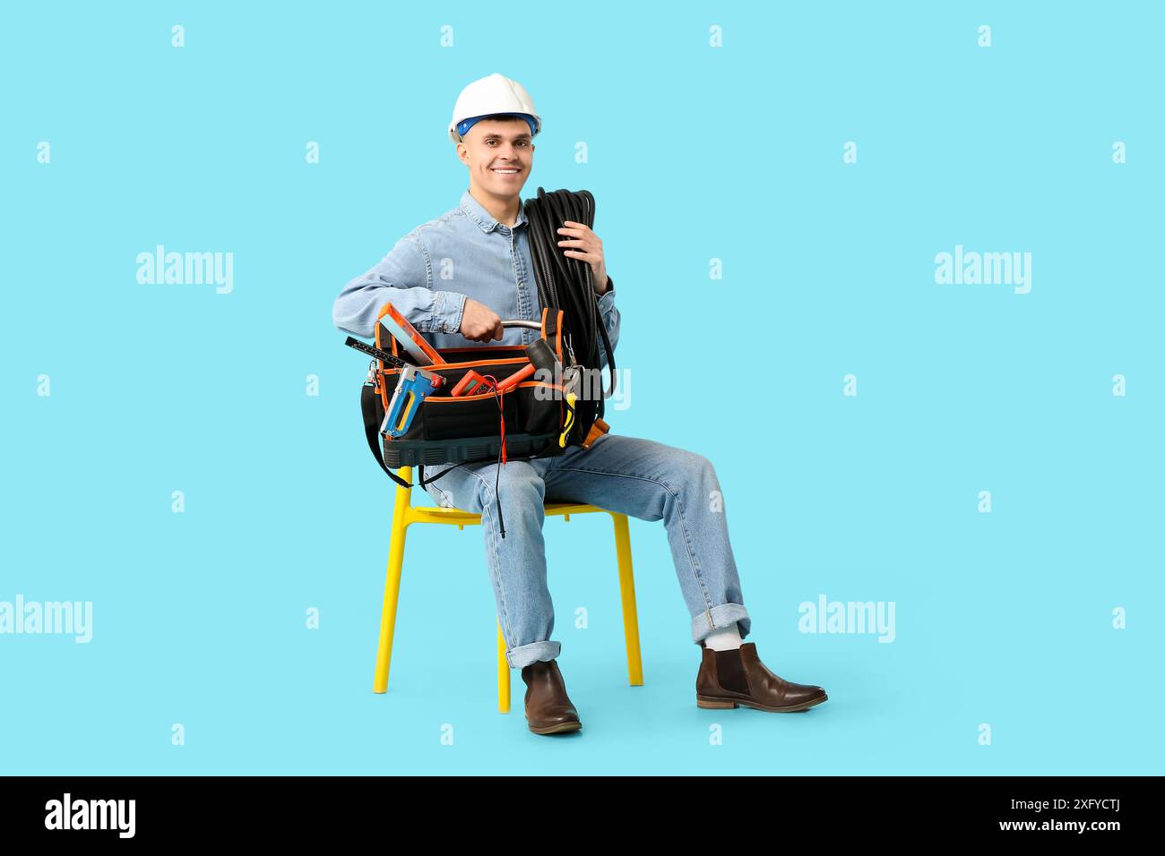 Young male electrician with tool bag and flexible conduit tube sitting ...