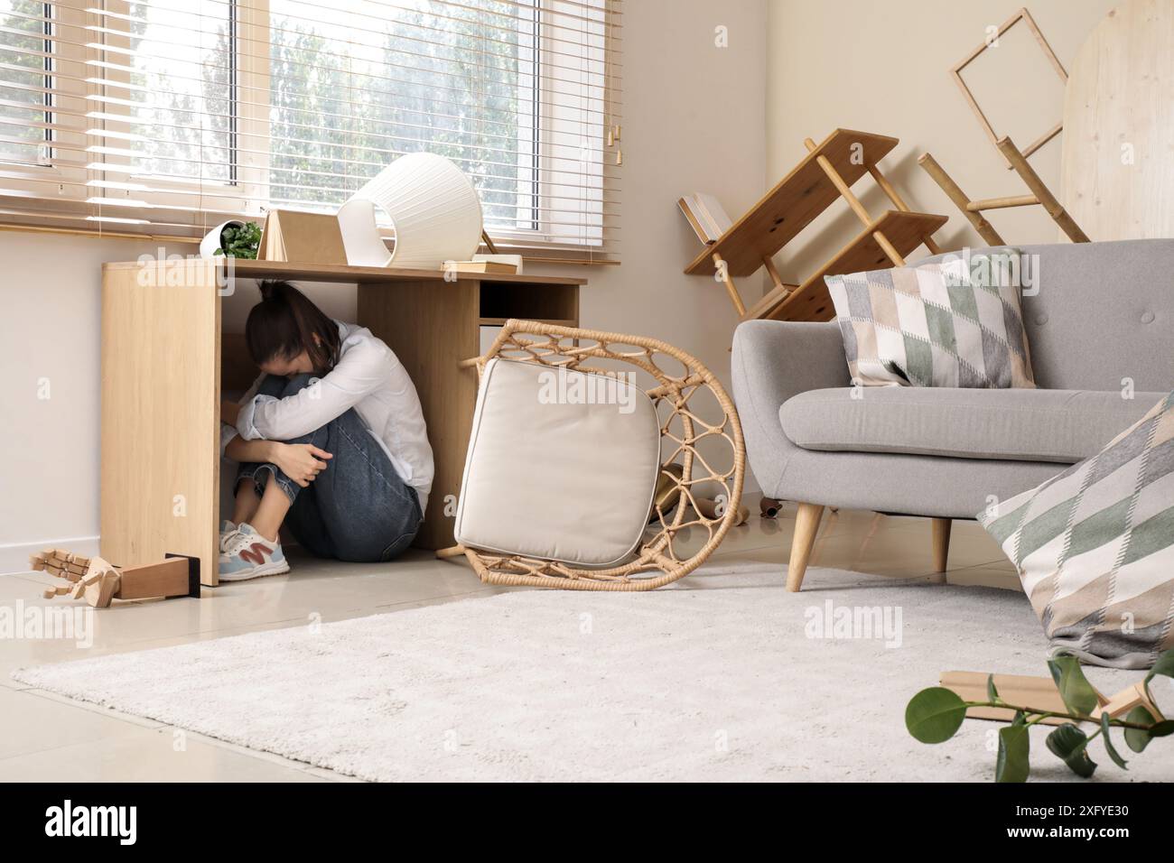 Scared young woman hiding under table in living room during earthquake ...