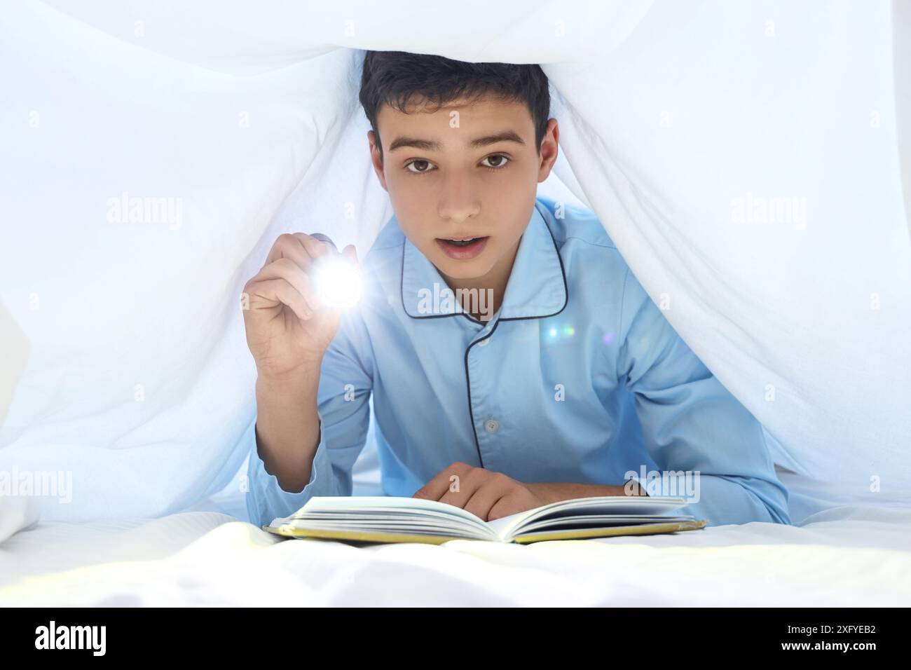 Teenage boy with shining flashlight reading book under blanket Stock ...