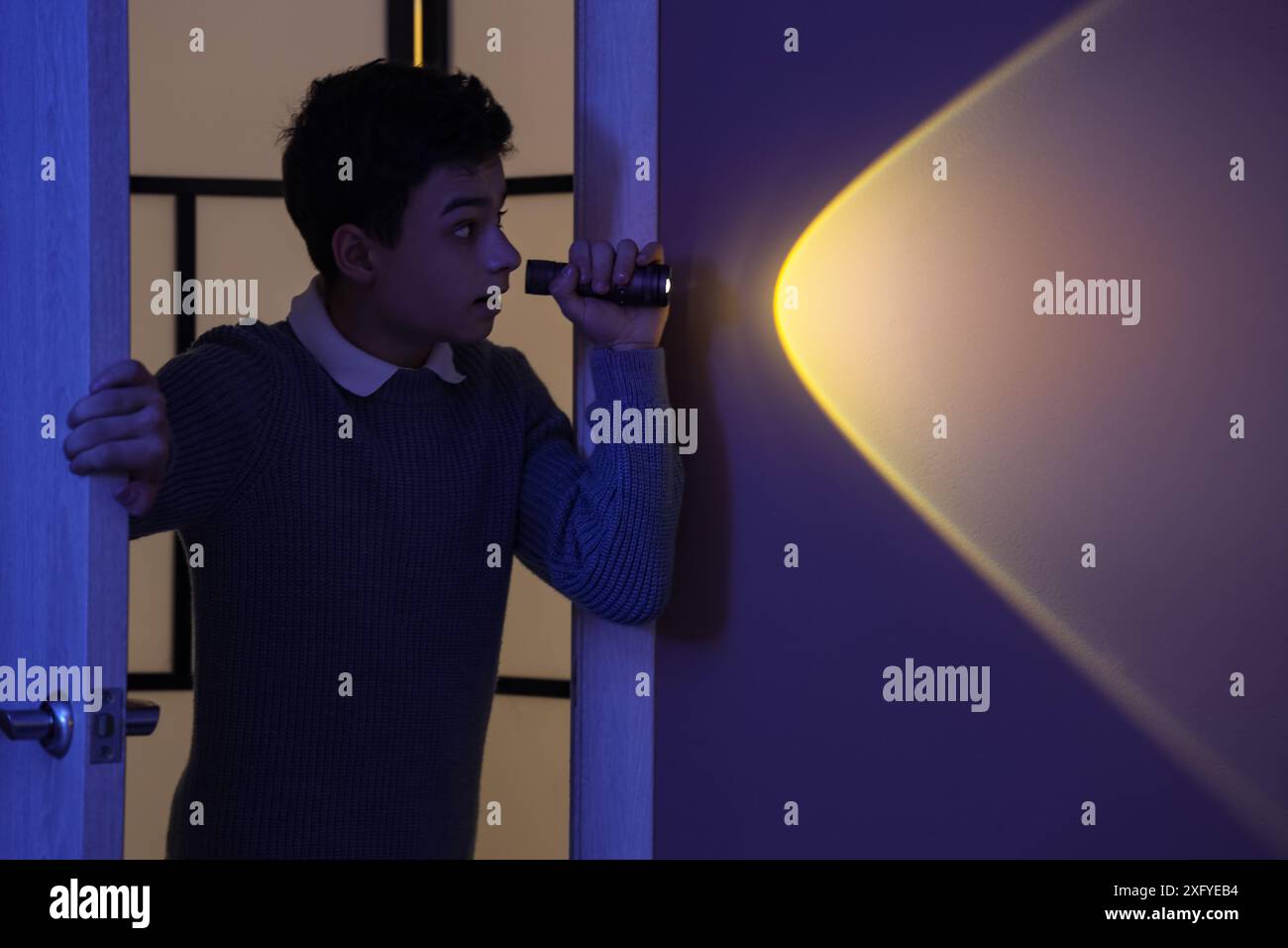 Teenage boy with shining flashlight walking through door in dark room ...