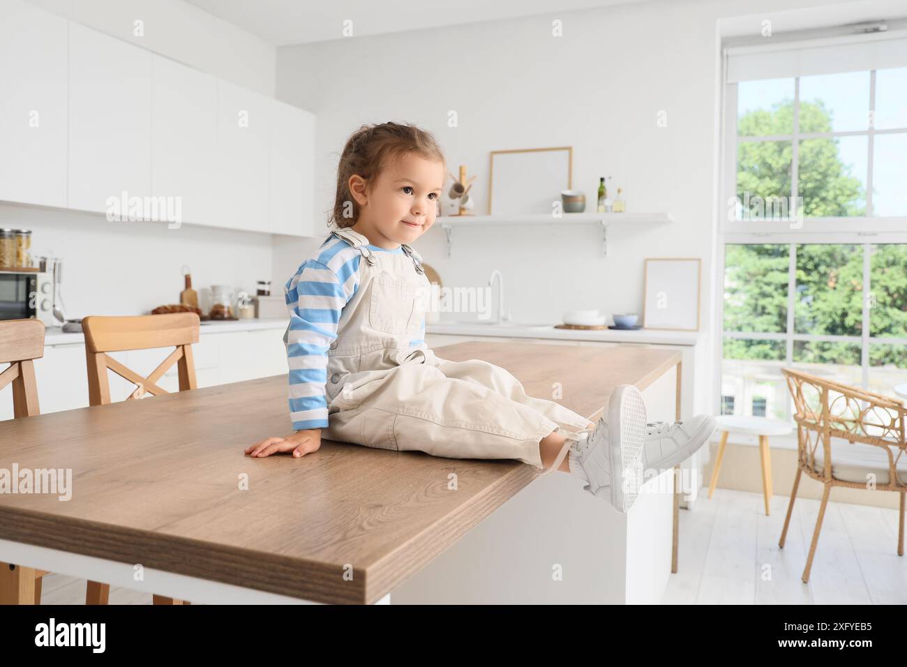 Cute little girl sitting on high table in kitchen. Child at risk Stock ...