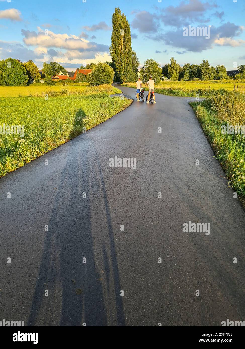 Two young cyclists take a short break on an empty road in a green ...