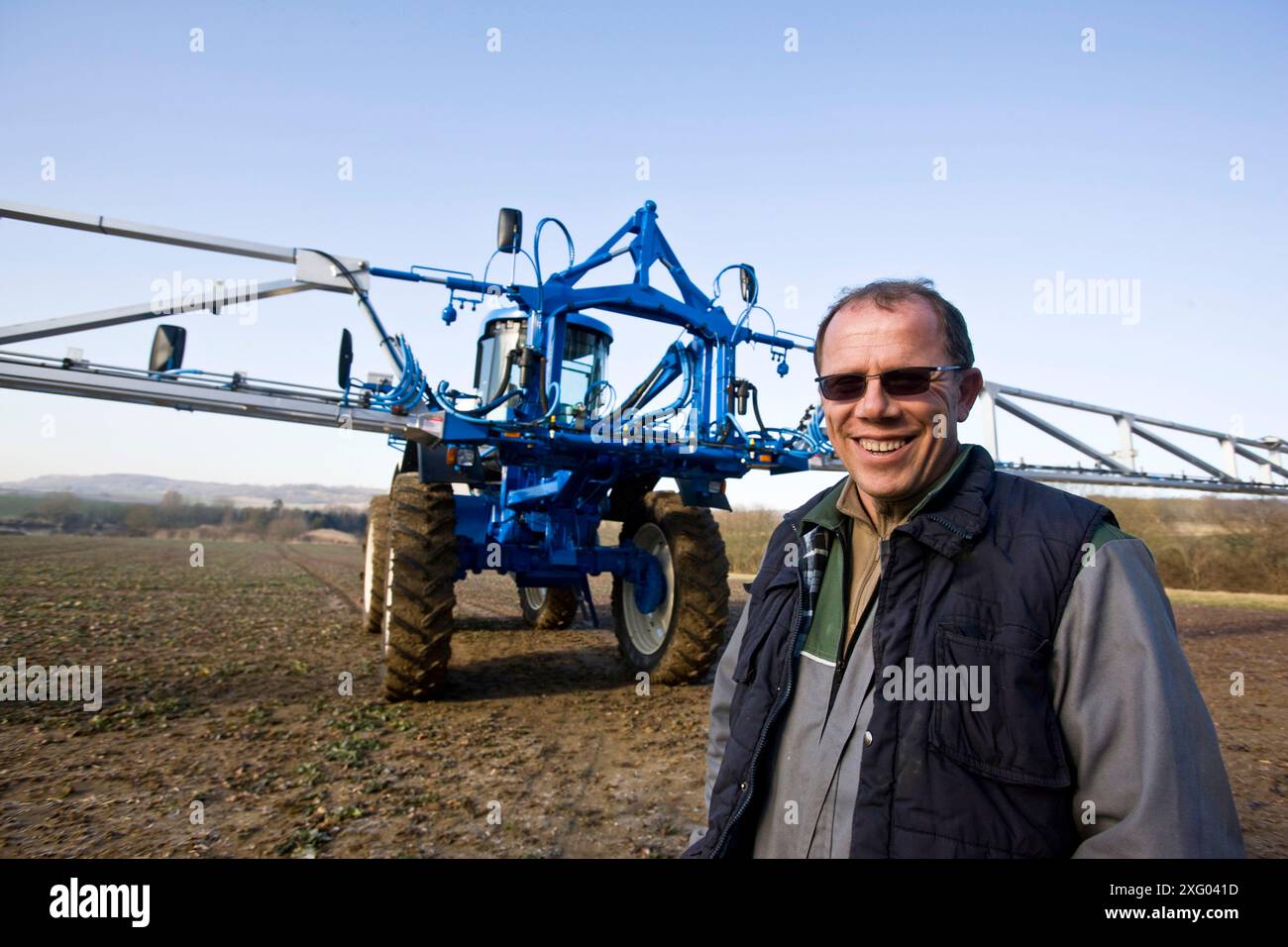 45-year-old farmer smiling in a field in front of his self-propelled ...